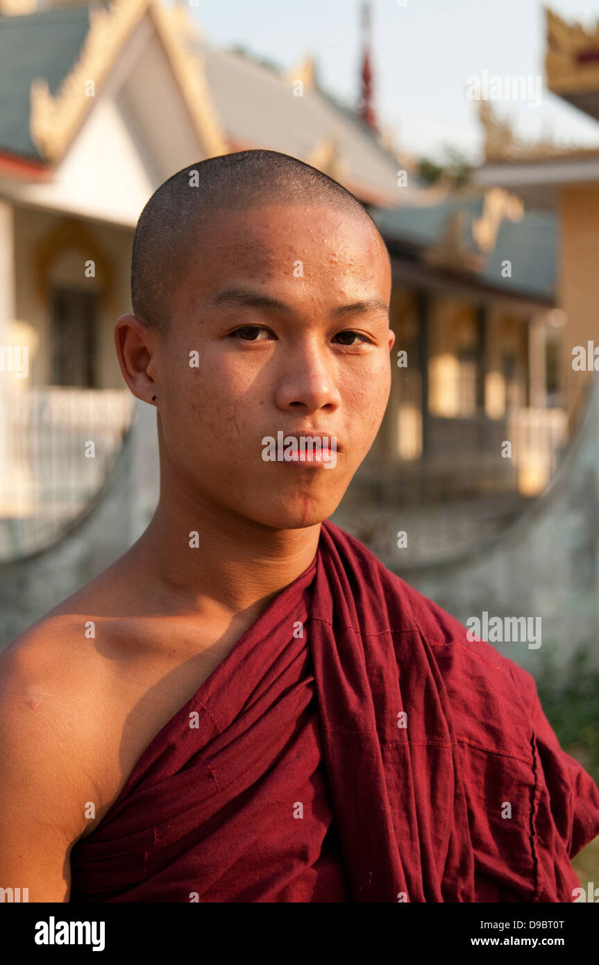 Teenage monk in red robes stands in front a temple Myanmar Burma Stock ...
