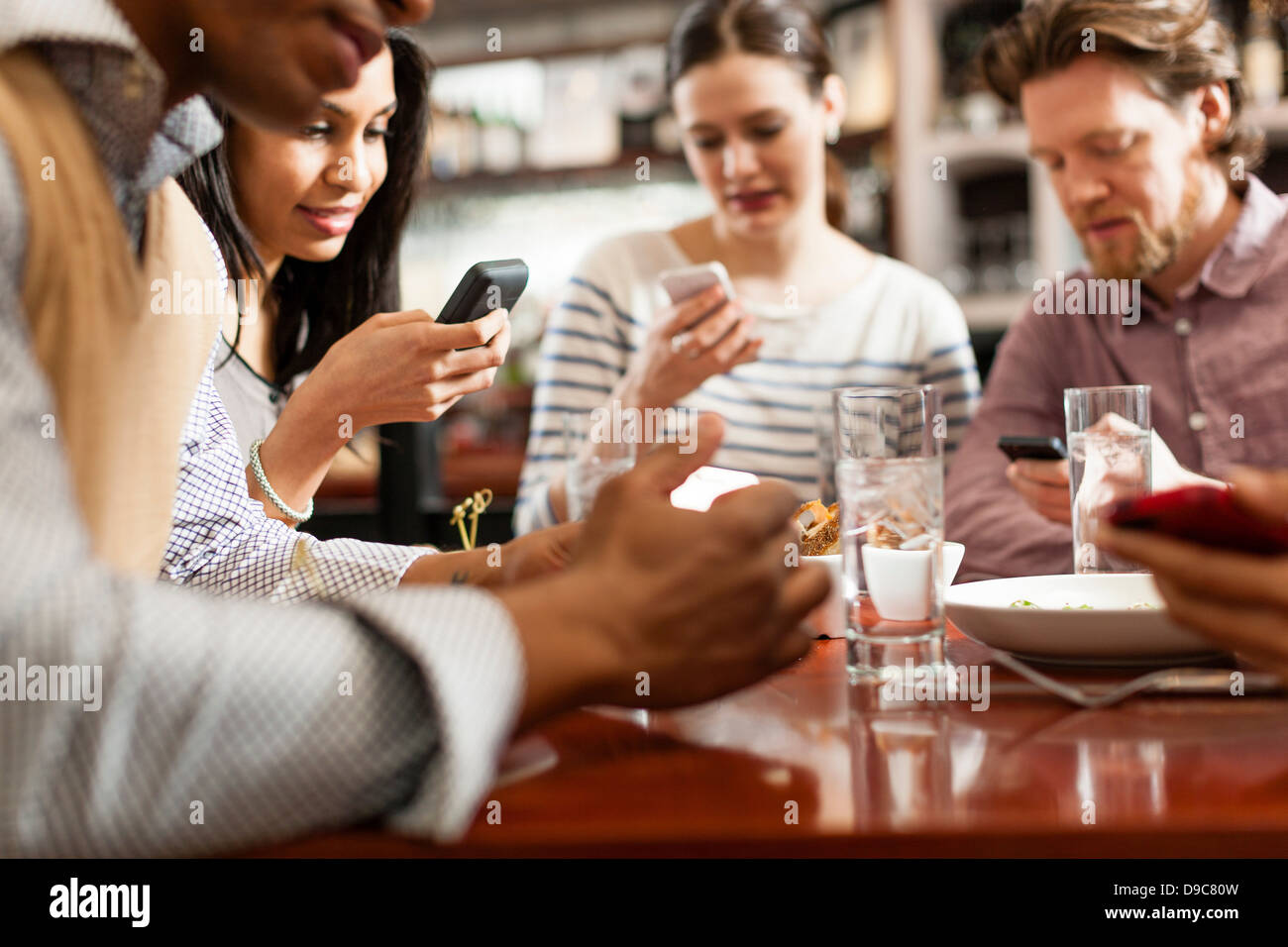 Friends at restaurant texting and showing photos using cell phones ...