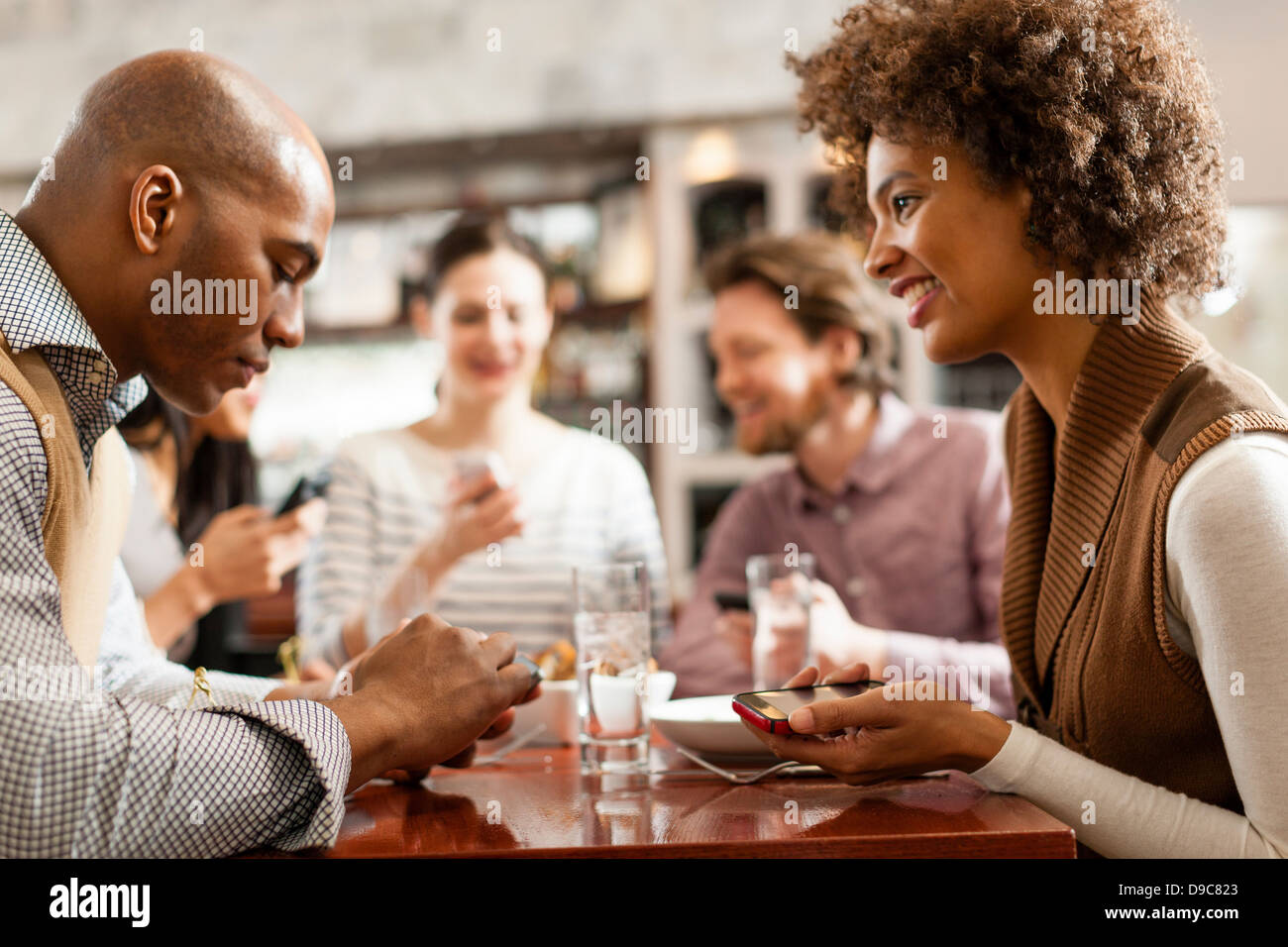 Friends at restaurant texting and showing photos using cell phones ...