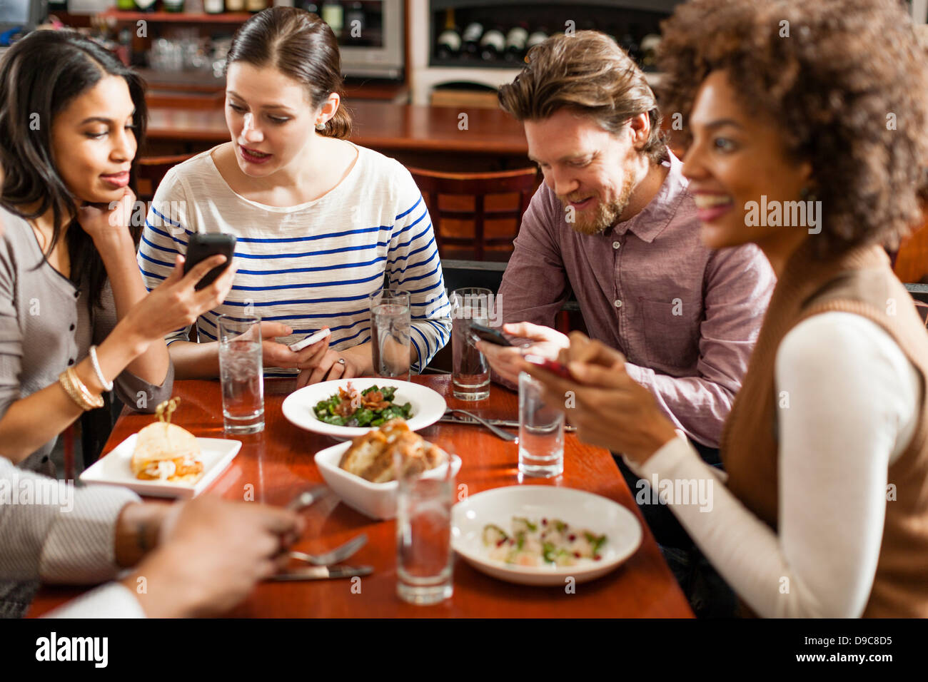 Friends at restaurant texting and showing photos using cell phones ...