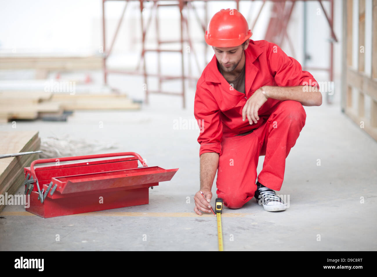 Builder with tool box and pencil measuring floor on construction site ...