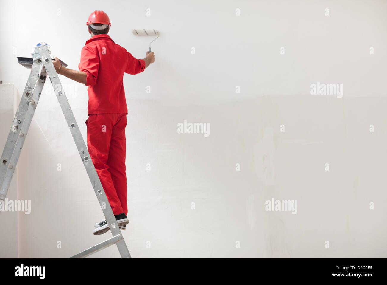 Decorator on step ladder painting white wall Stock Photo - Alamy