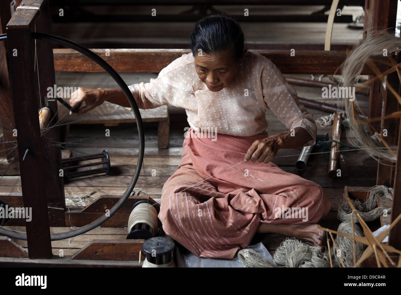 Older woman spinning Lotus Flower Fibers on wooden spinning wheel in ...