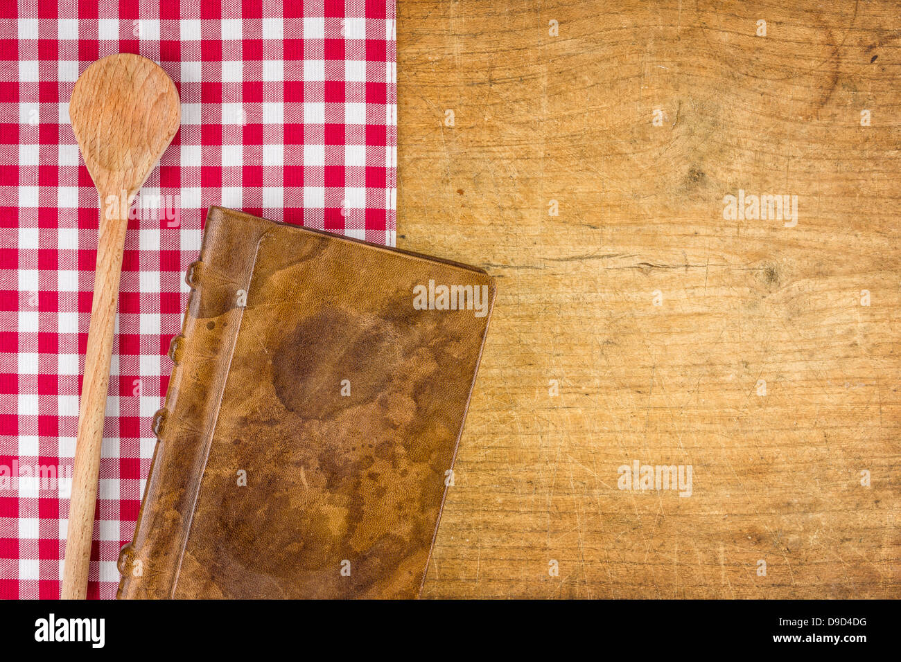 Wooden spoon and book on a wooden board with a checkered tablecloth ...