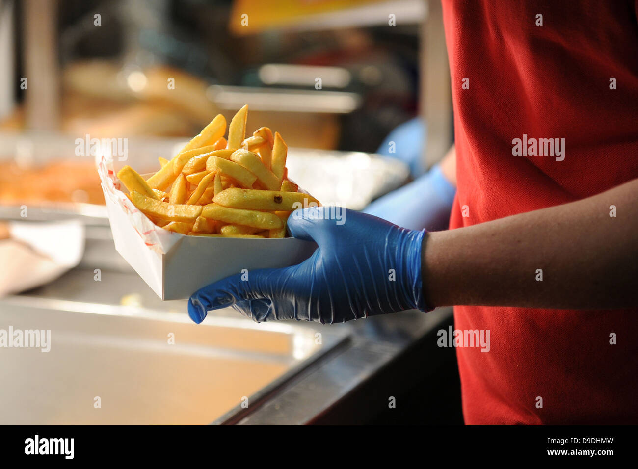 A chip shop worker wearing blue gloves holding a tray of freshly fried ...