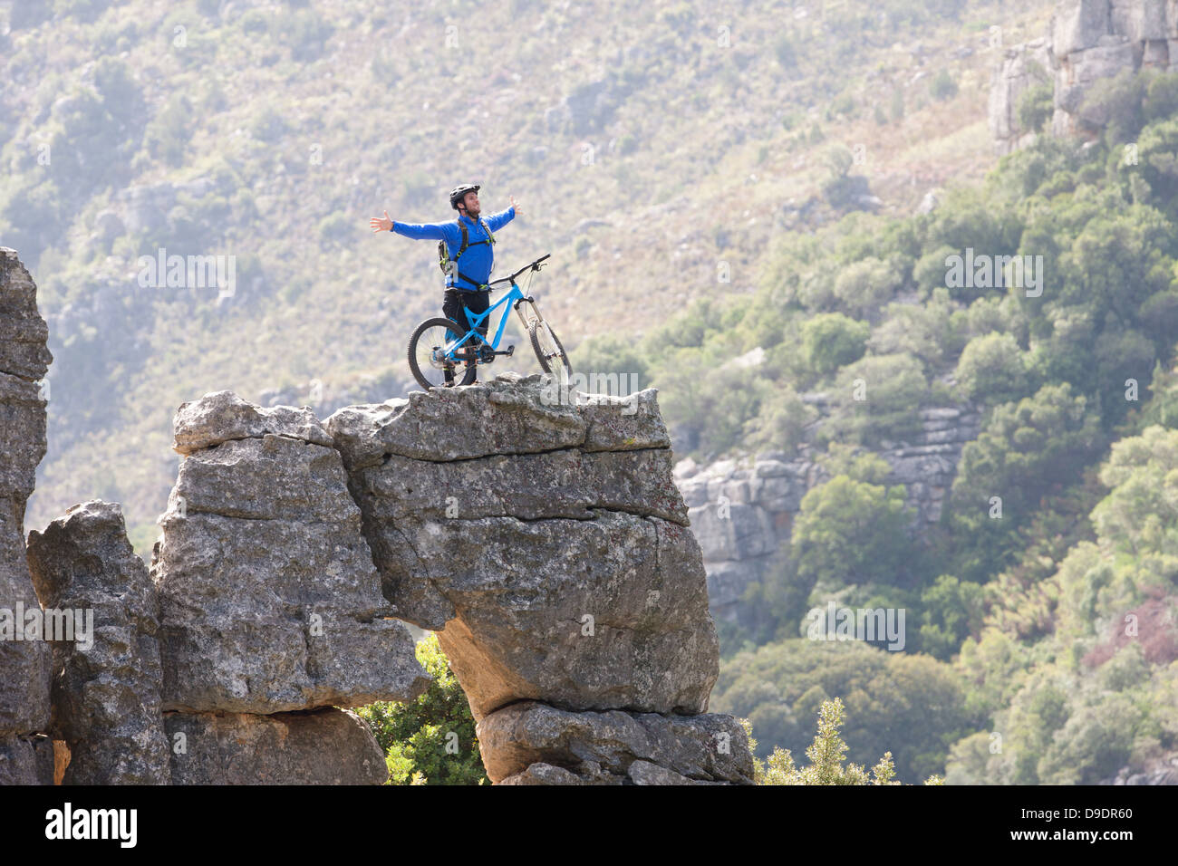 Young man with mountain bike and arms outstretched on rock Stock Photo ...
