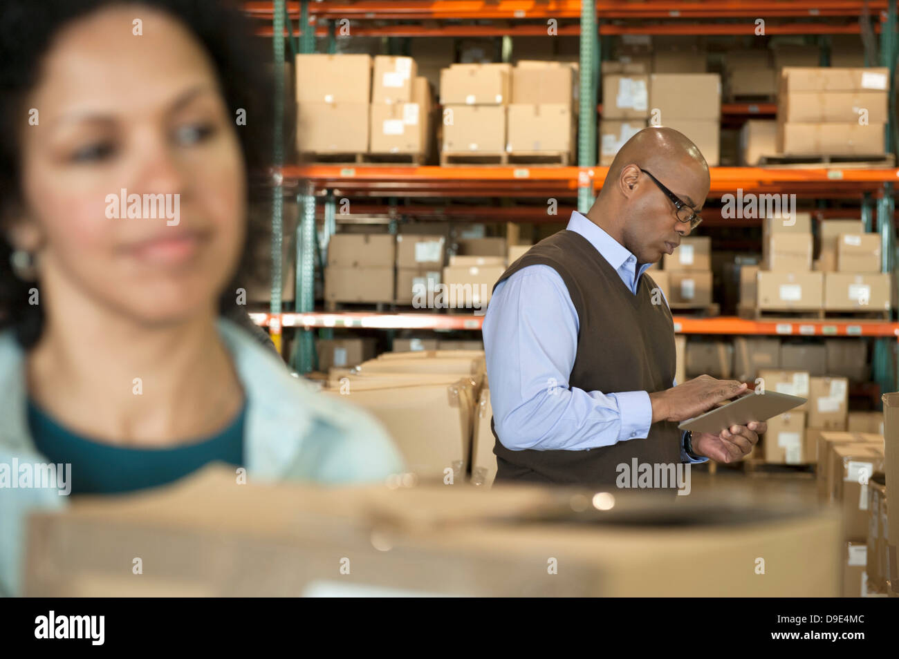 Male warehouse manager using digital tablet, woman in foreground Stock ...