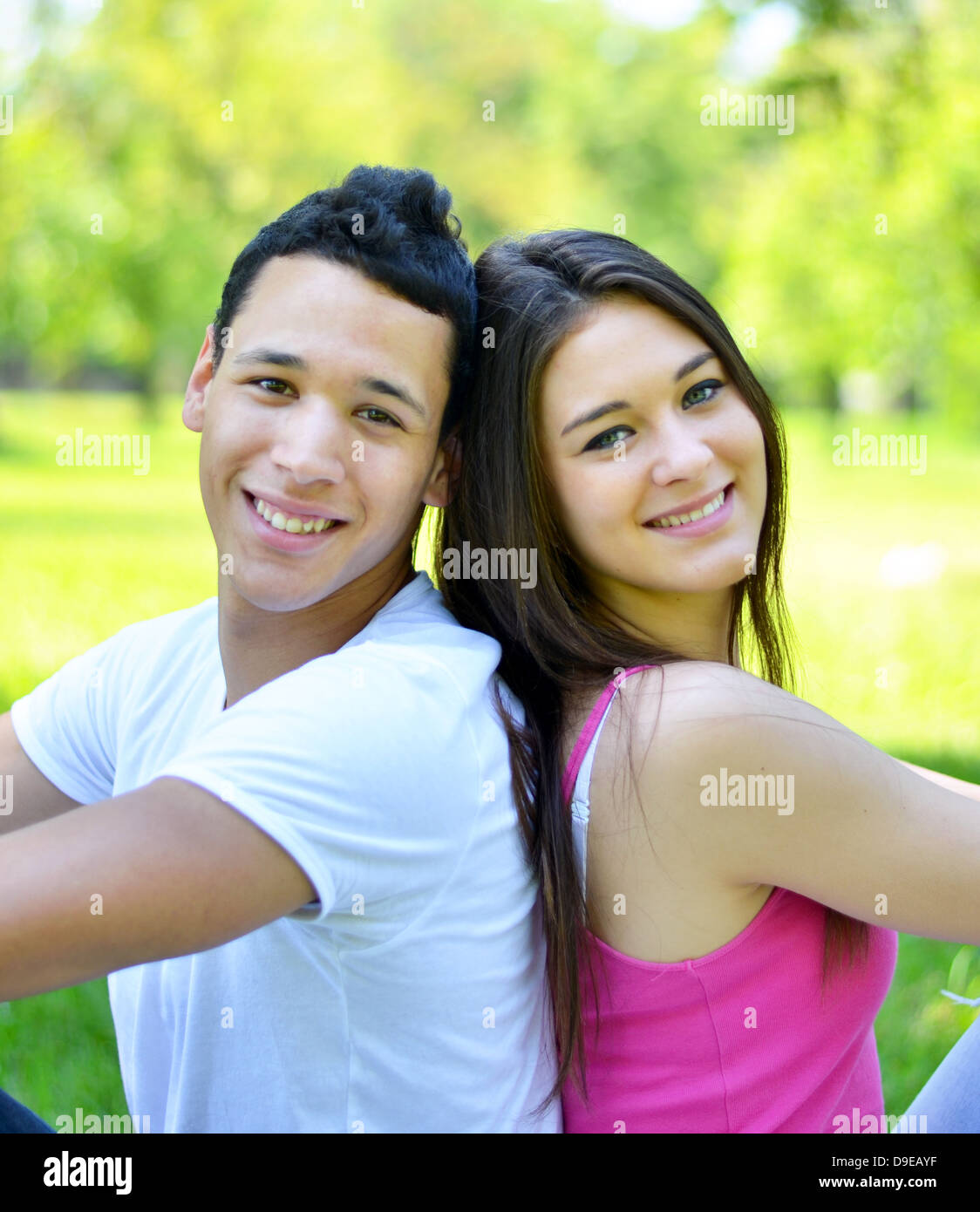 Happy young couple back to back in park Stock Photo - Alamy