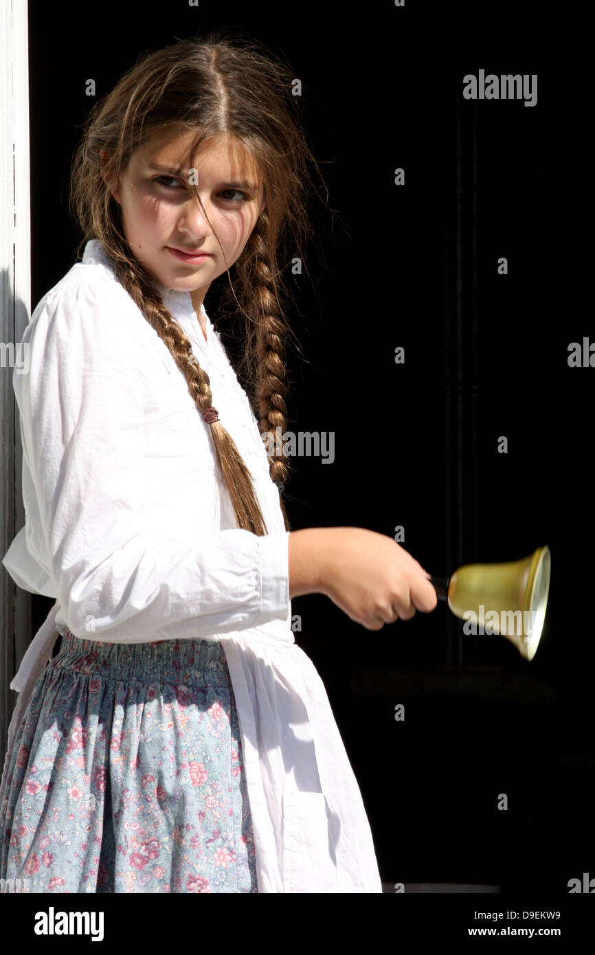A young girl ringing the hand bell for a historical one room school to ...
