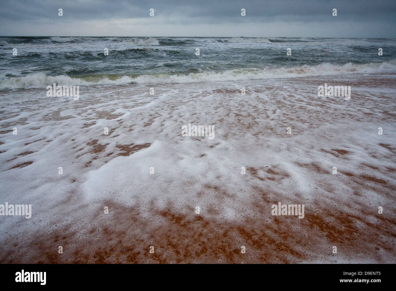 Heavy surf and waves fill the beach with patterns of white foam along a ...