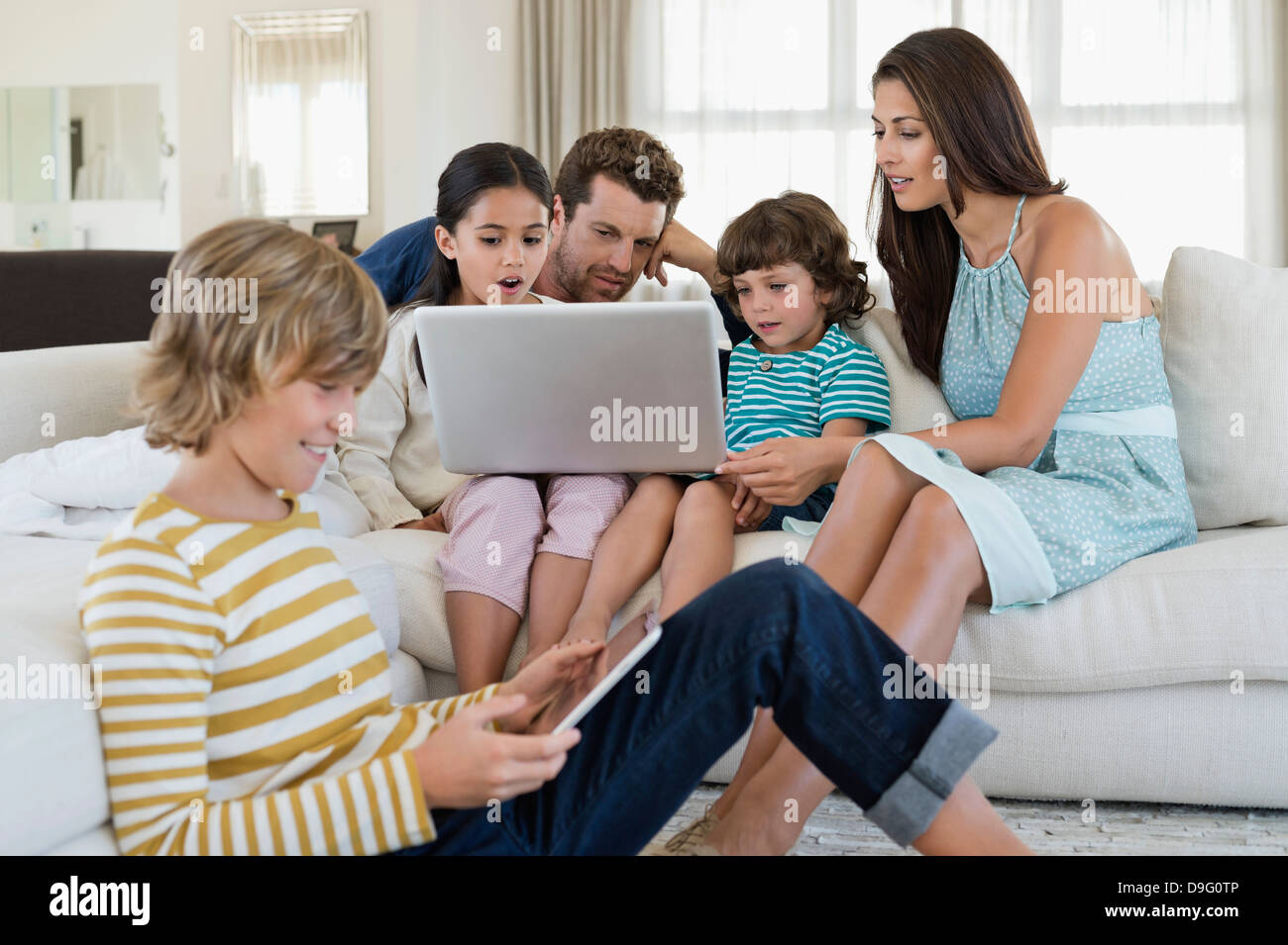 Family using electronic gadgets in a living room Stock Photo - Alamy