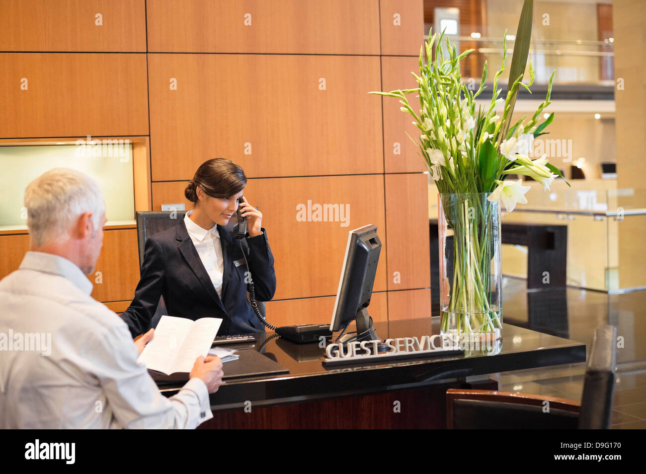 Businessman reading a brochure with a receptionist talking on a ...