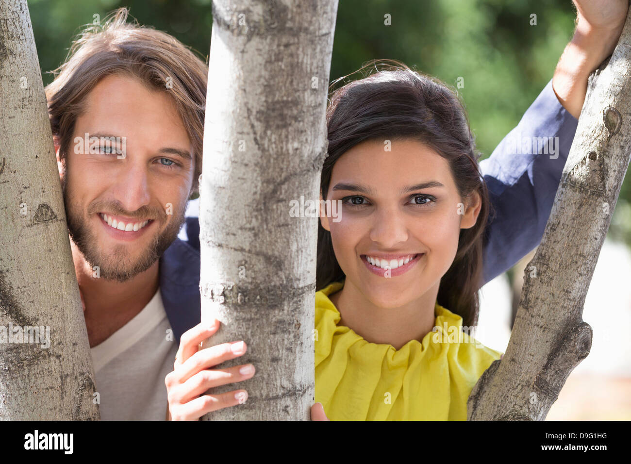 Portrait of a couple smiling behind a tree Stock Photo - Alamy