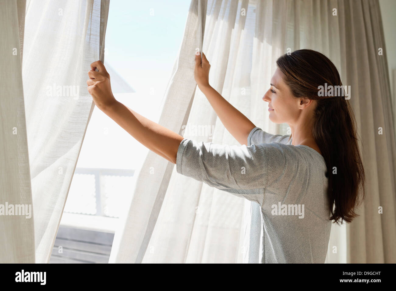 Woman opening the curtain of a window Stock Photo - Alamy