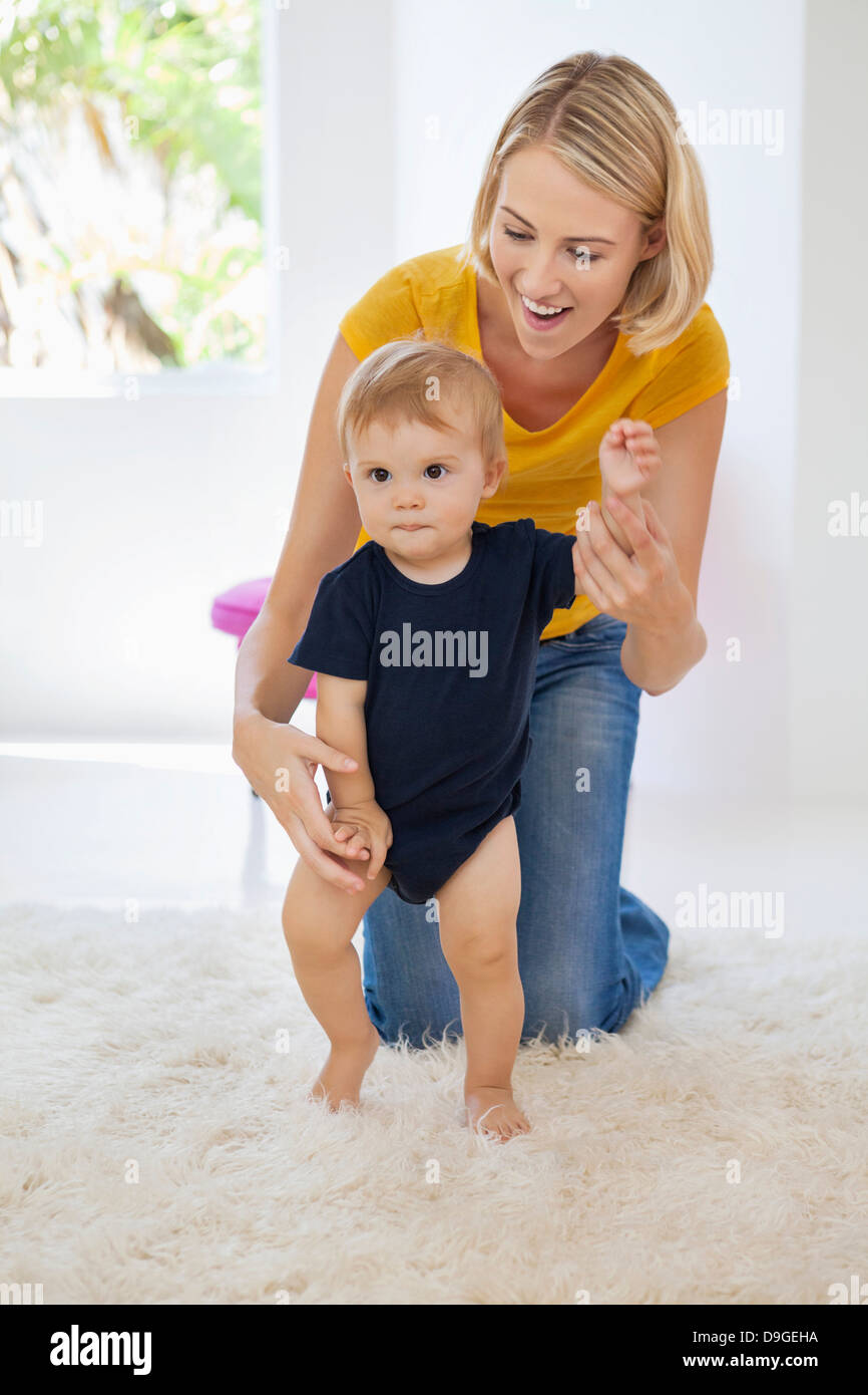 Smiling mother helping her baby to walk Stock Photo - Alamy