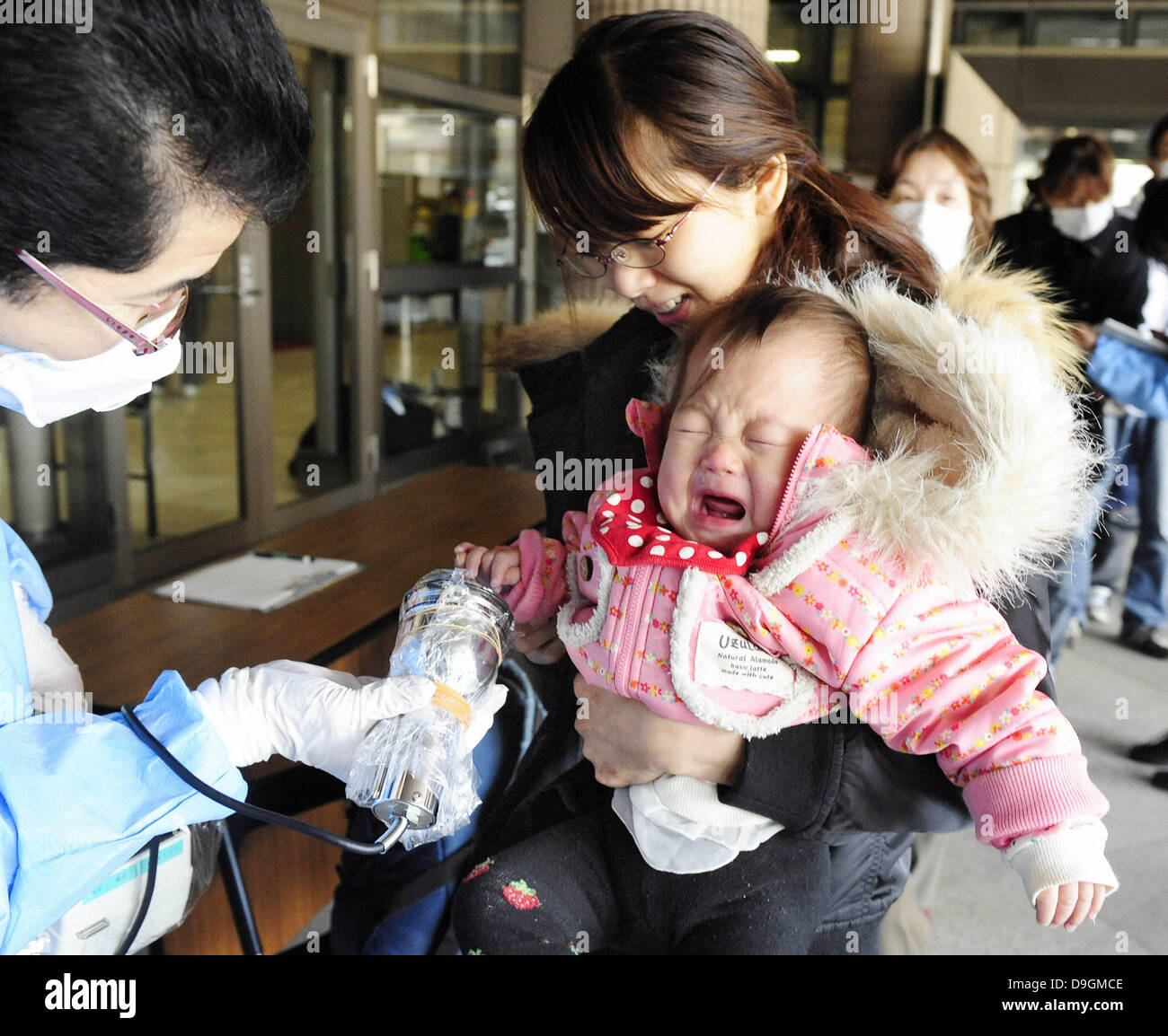 A baby cries as she gets screened for radiation in front of an ...