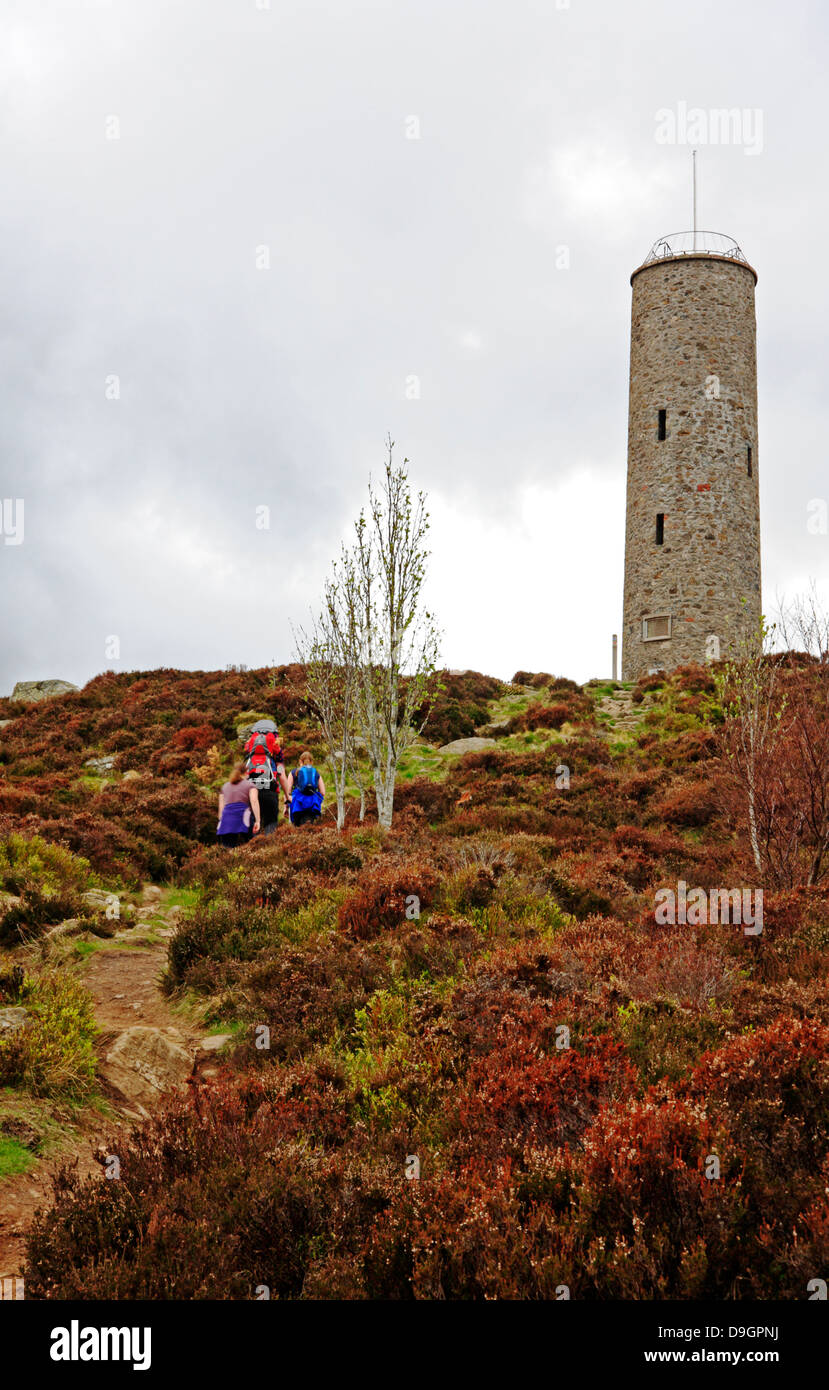 Three hill walkers nearing the top of Scolty Hill and the stone tower ...
