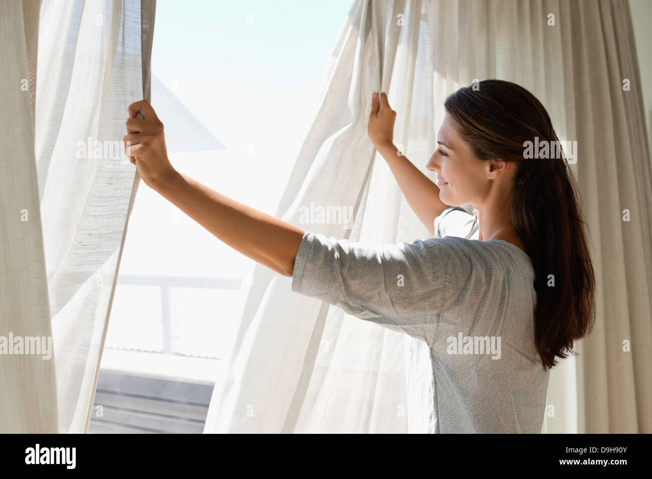 Woman opening the curtain of a window Stock Photo - Alamy