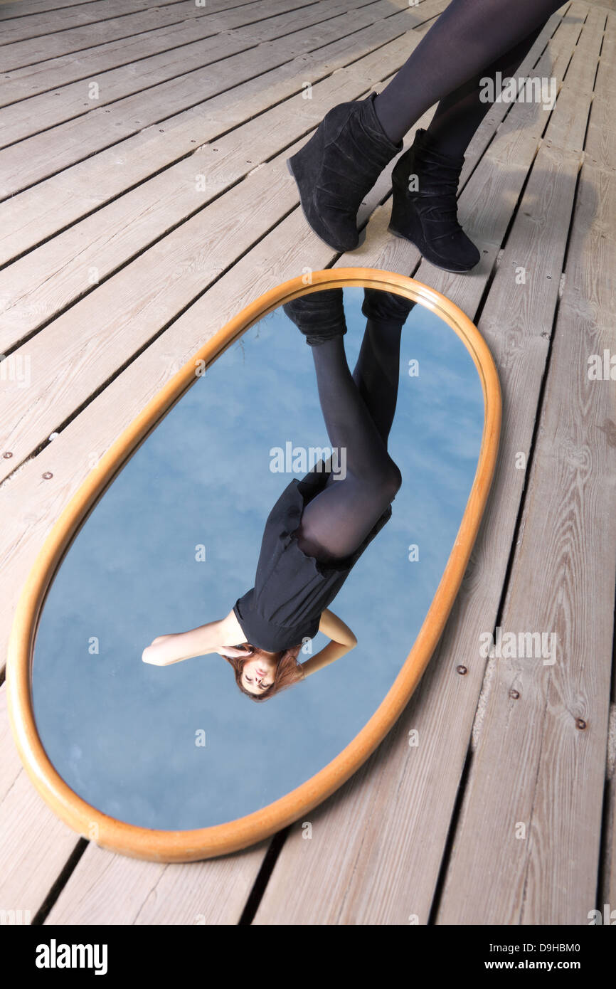 thoughtful young woman in black with her reflection in mirror ...