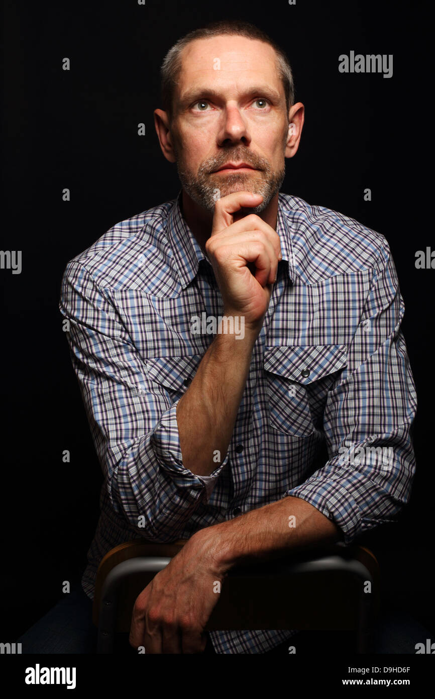 A dramatic portrait of a 40-something male looking up with hand on chin ...