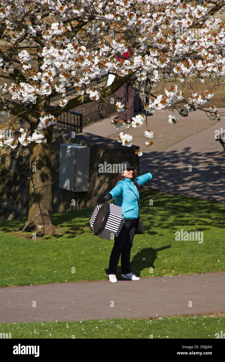 Woman with arms outstretched holding hat boxes under blossom tree at ...