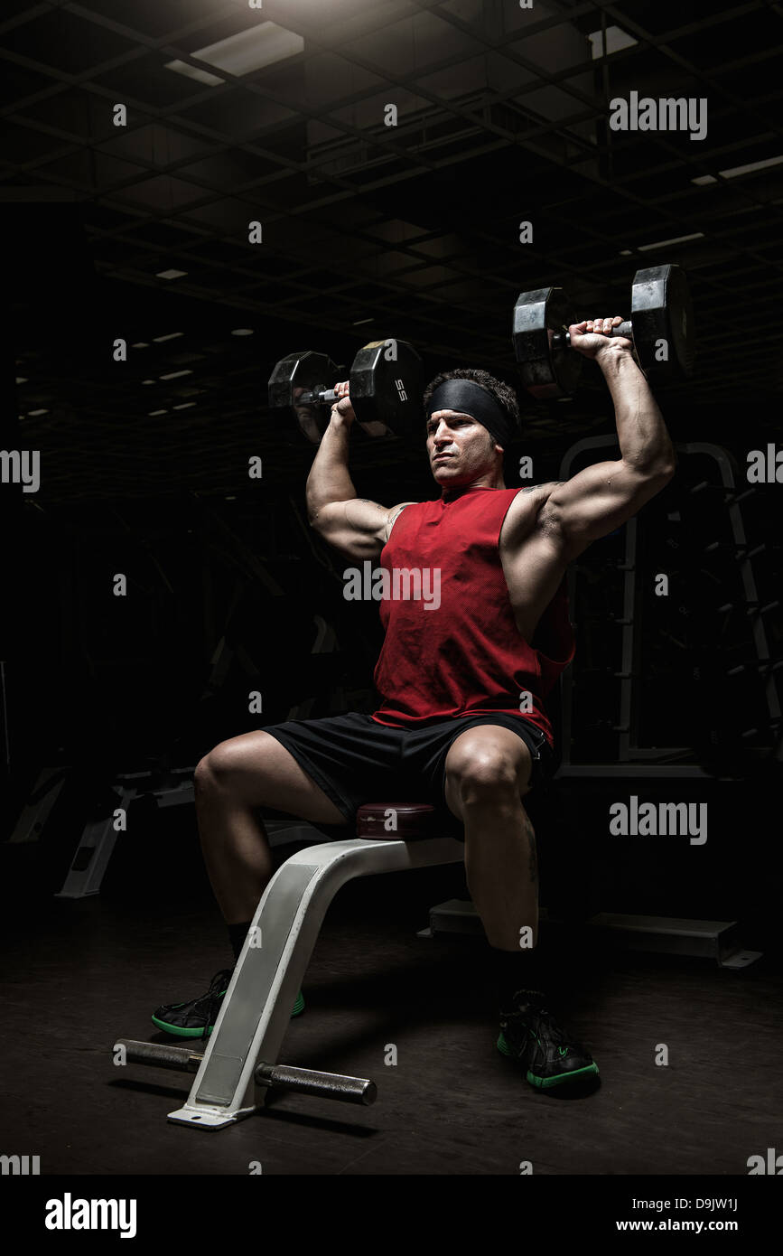 Muscular young man performing shoulder raises with dumbbells in gym ...