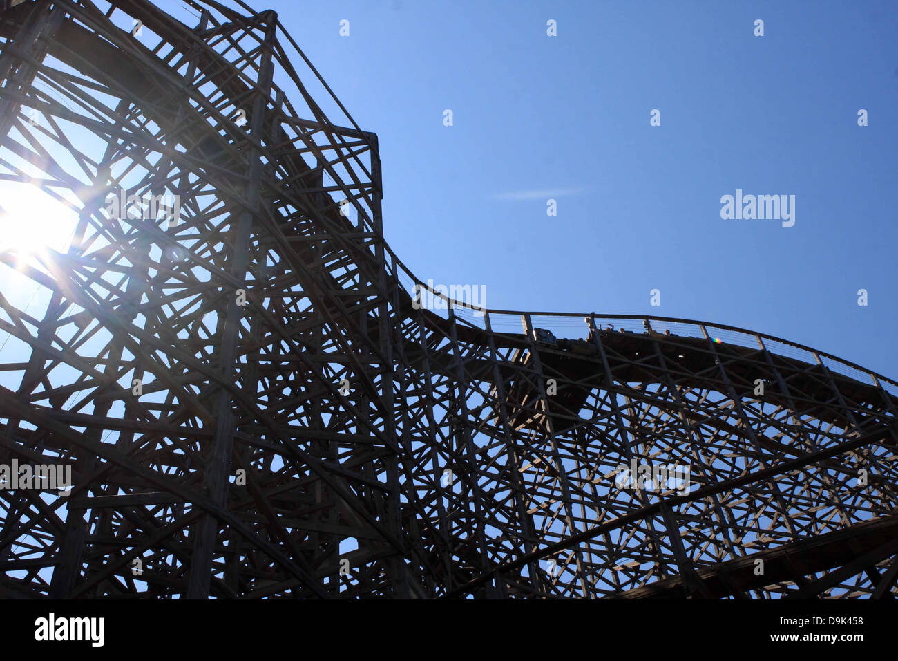 Looking up at a wooden roller coaster silhouette in the sun and blue ...