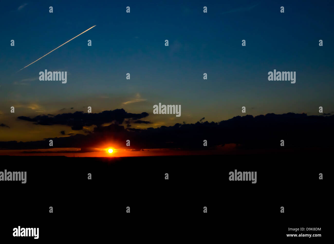 Orange glow of the sun surrounded by clouds in a dark sky at sunset. A ...