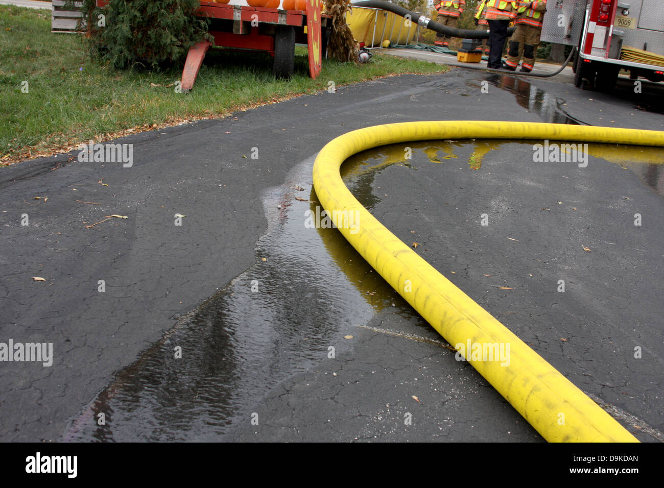 Firefighters working a fire scene with a large yellow pumper hose from ...