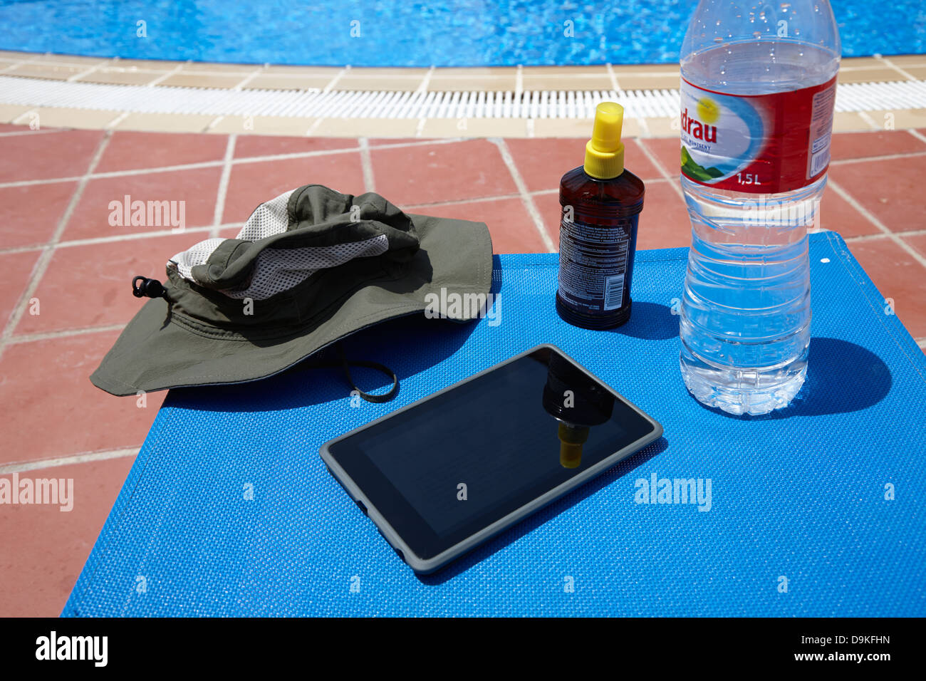 hat tablet computer water and sunscreen by the side of a swimming pool ...