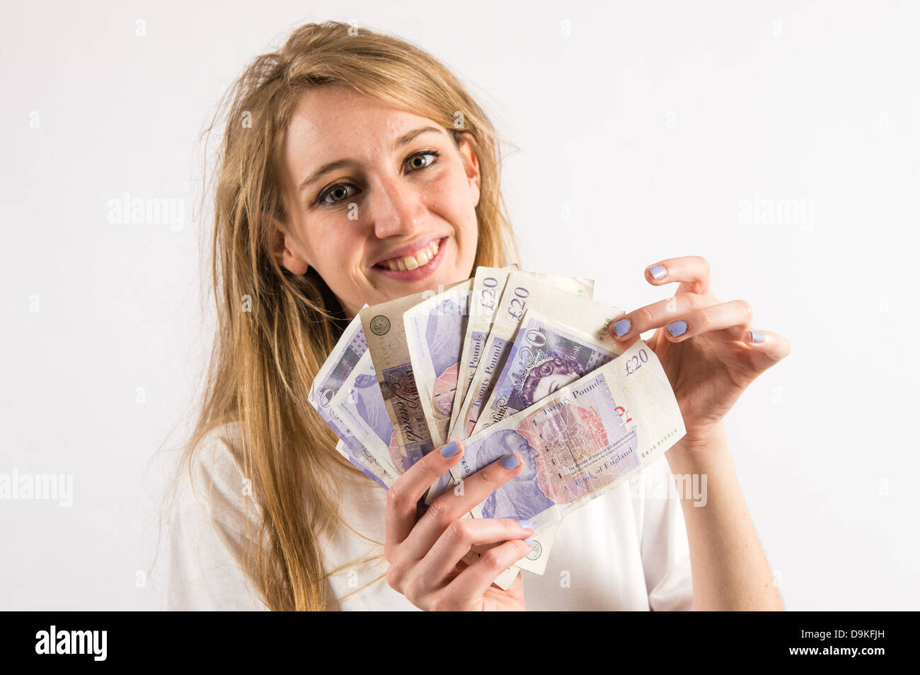 A young woman holding a fan handful of UK sterling money cash £20 notes ...