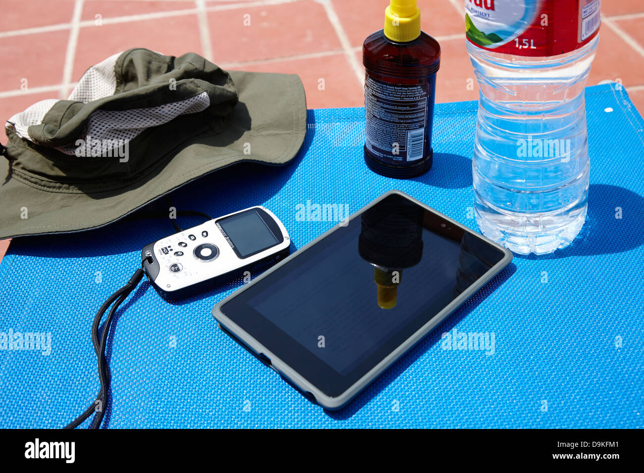 hat tablet computer, camera, water and sunscreen by the side of a ...