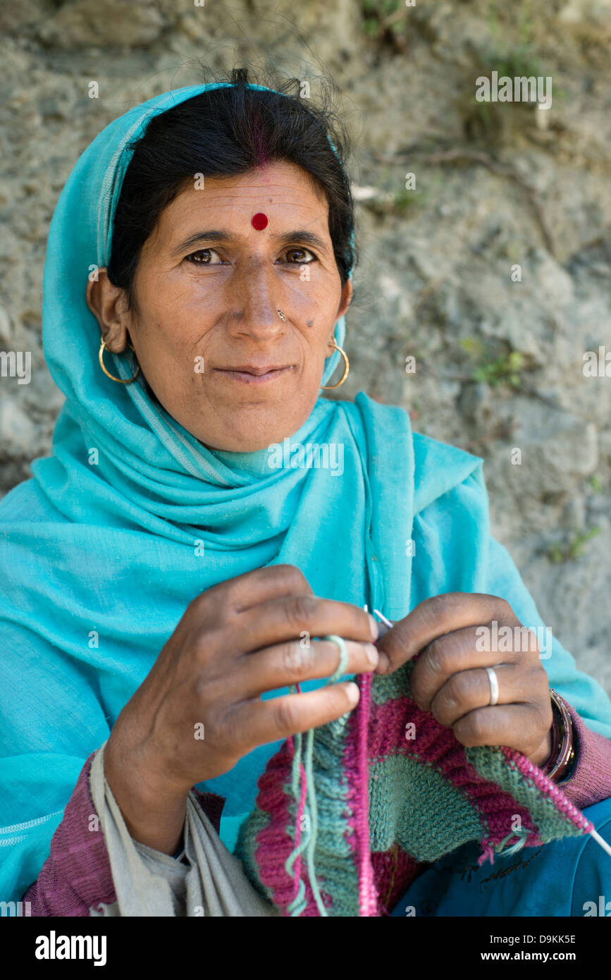 A Gaddi tribeswoman knits a garment while posing for the camera at the ...