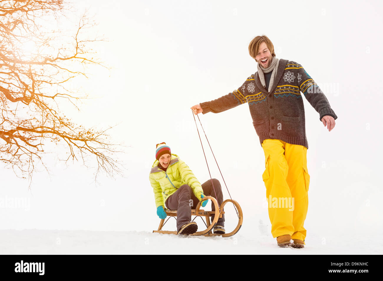 Man pulling woman through snow on toboggan Stock Photo - Alamy