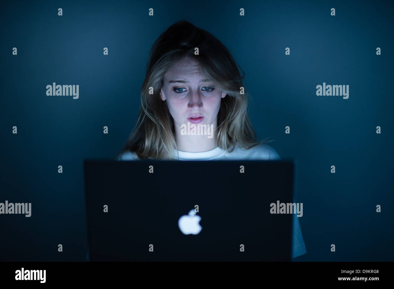 A young woman using a Apple laptop computer - looking scared worried ...