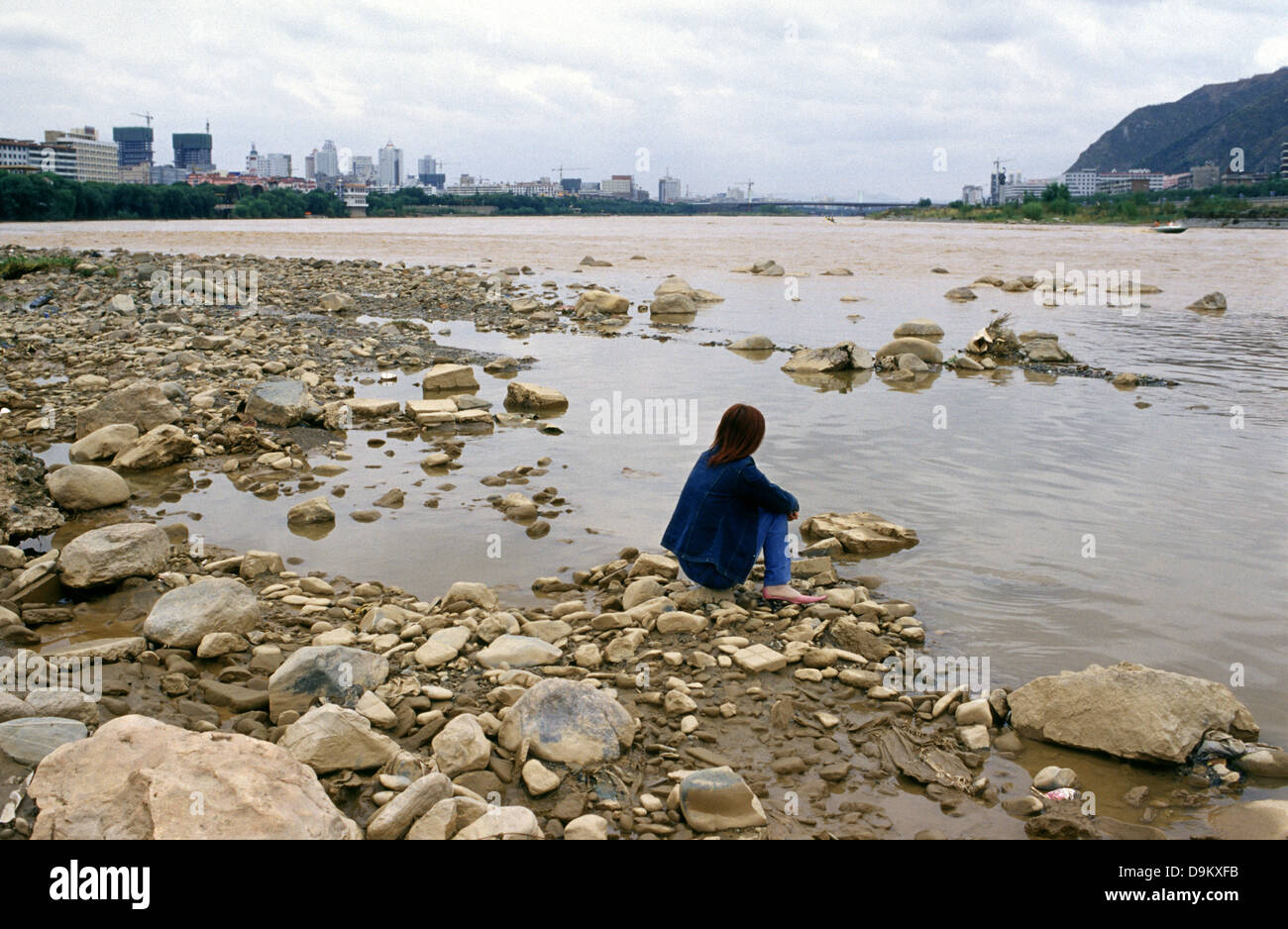 Lone young Chinese woman siting at the shore of the Huang He Yellow ...