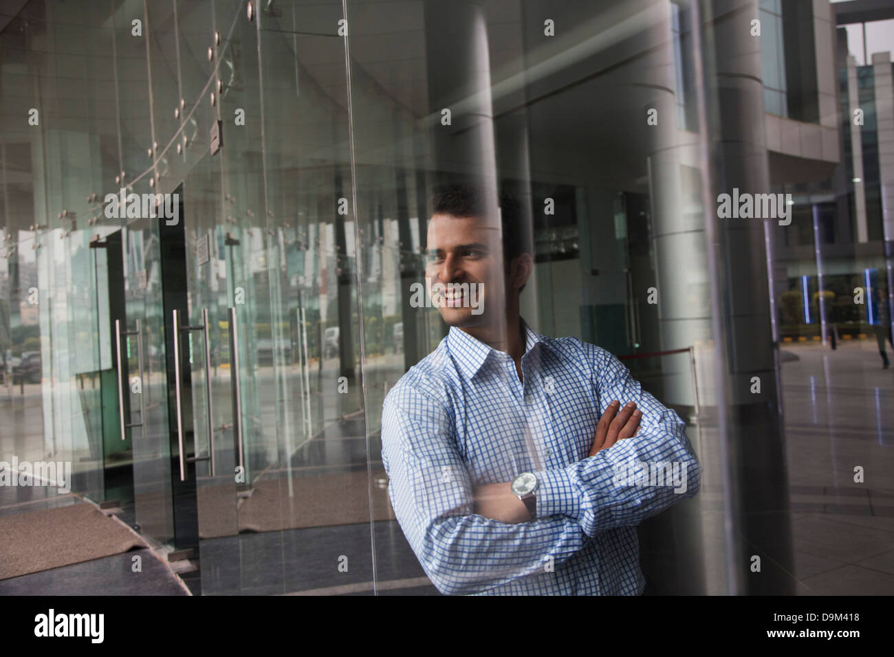 Businessman leaning against a glass wall in office Stock Photo - Alamy