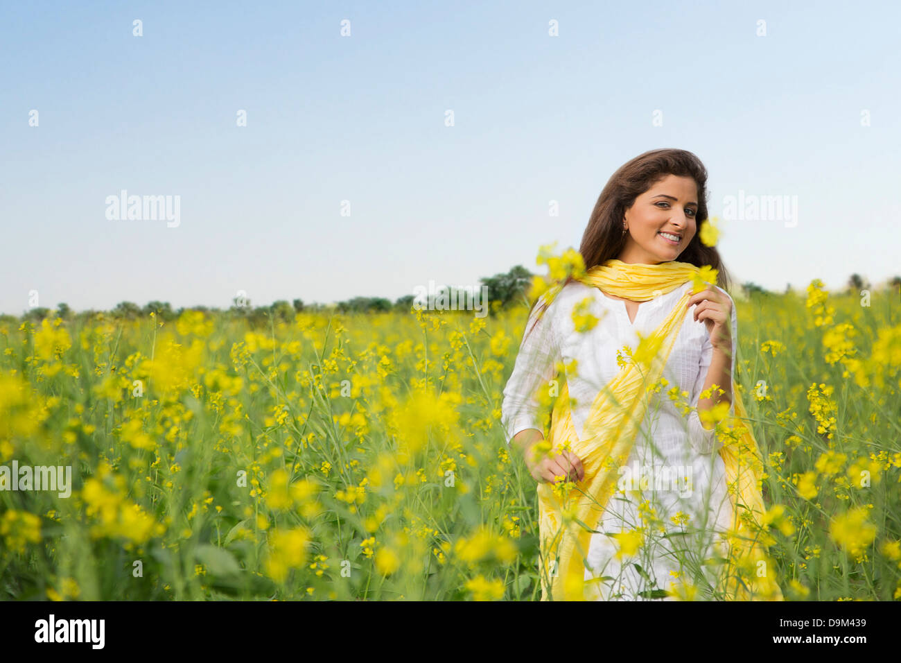 Woman standing in a mustard field and smiling Stock Photo - Alamy