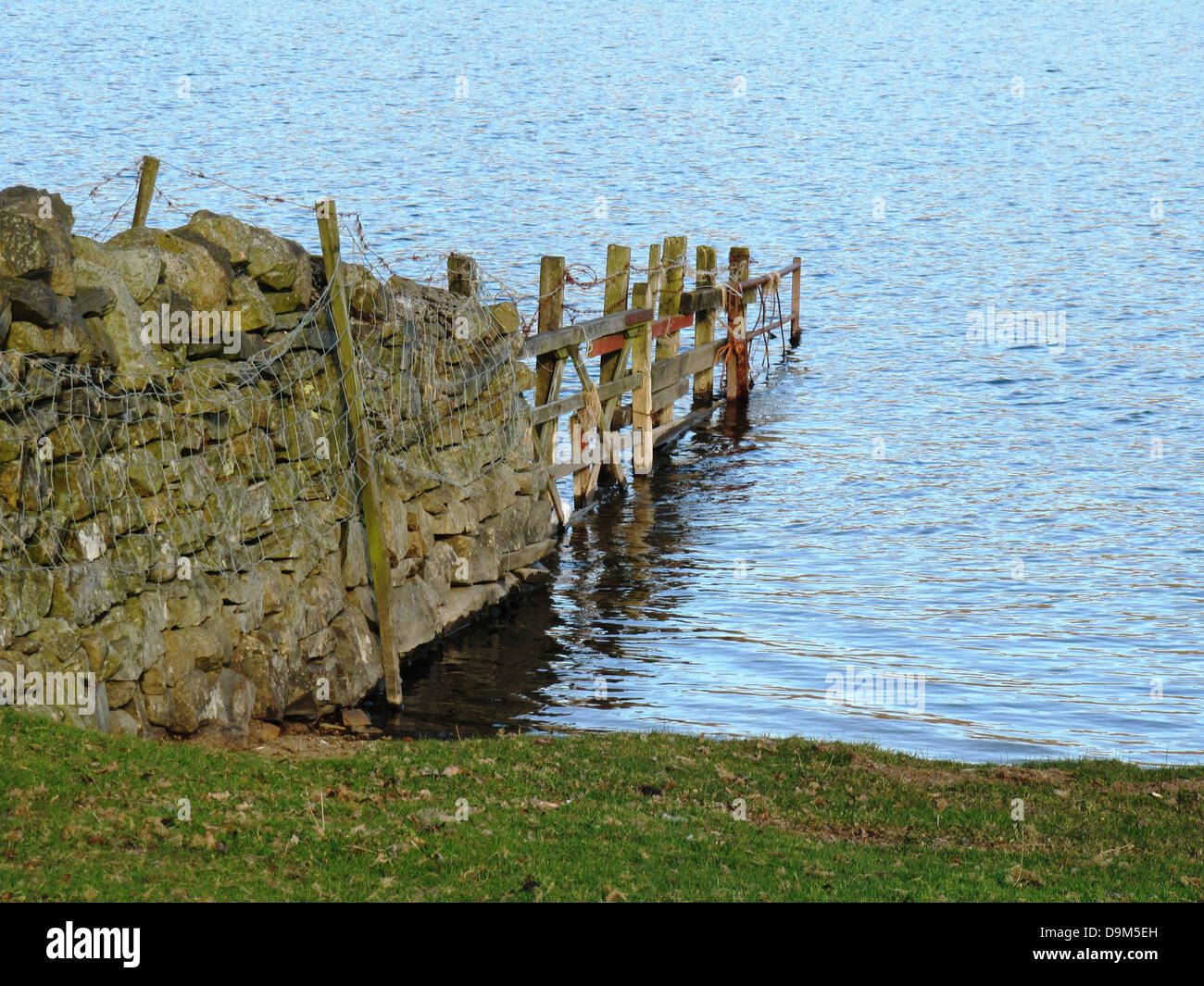 A stone wall and wooden fence protruding into a lake Stock Photo - Alamy