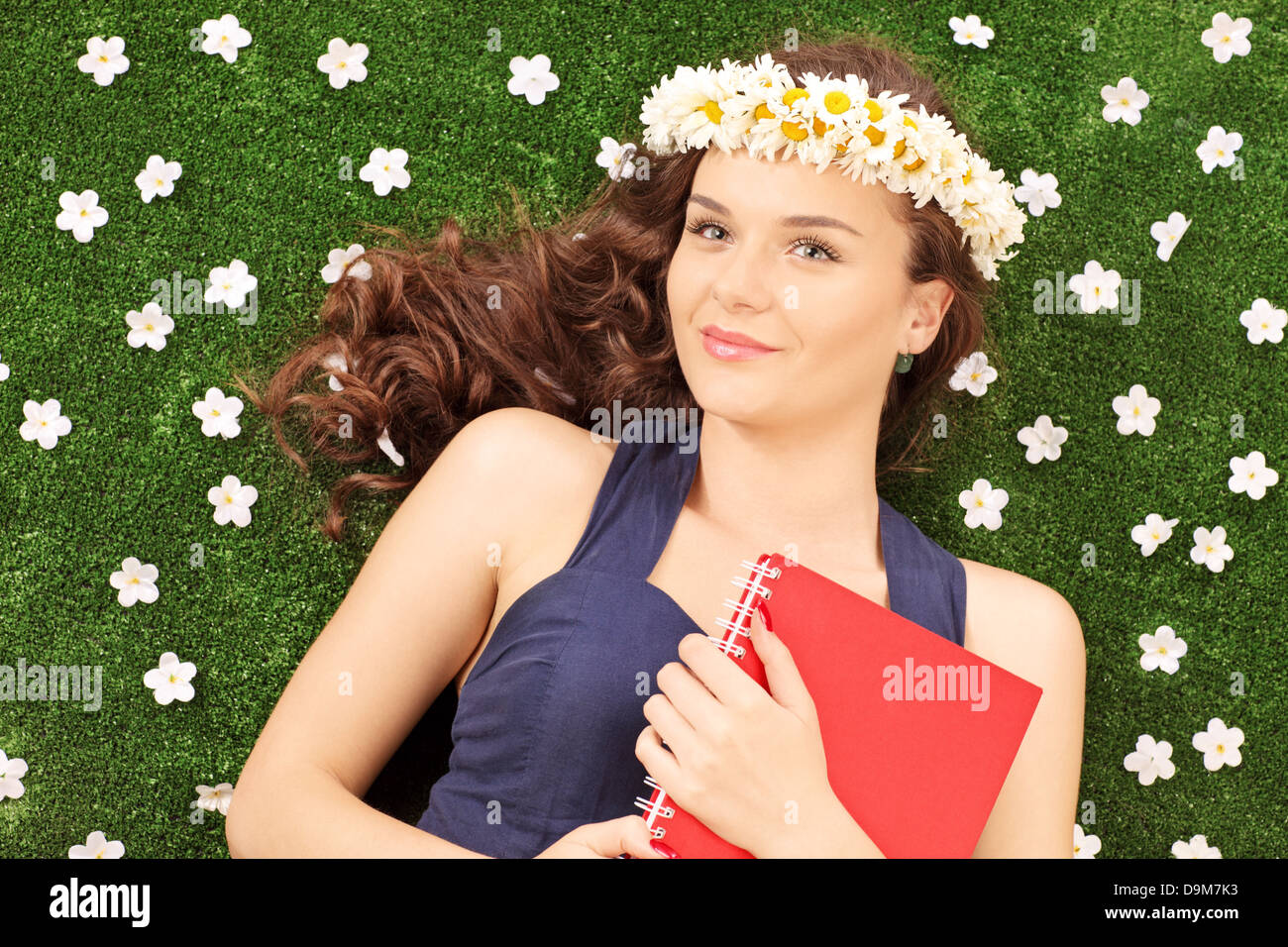 Beautiful young woman with a daisy hair wreath lying on a grass with ...