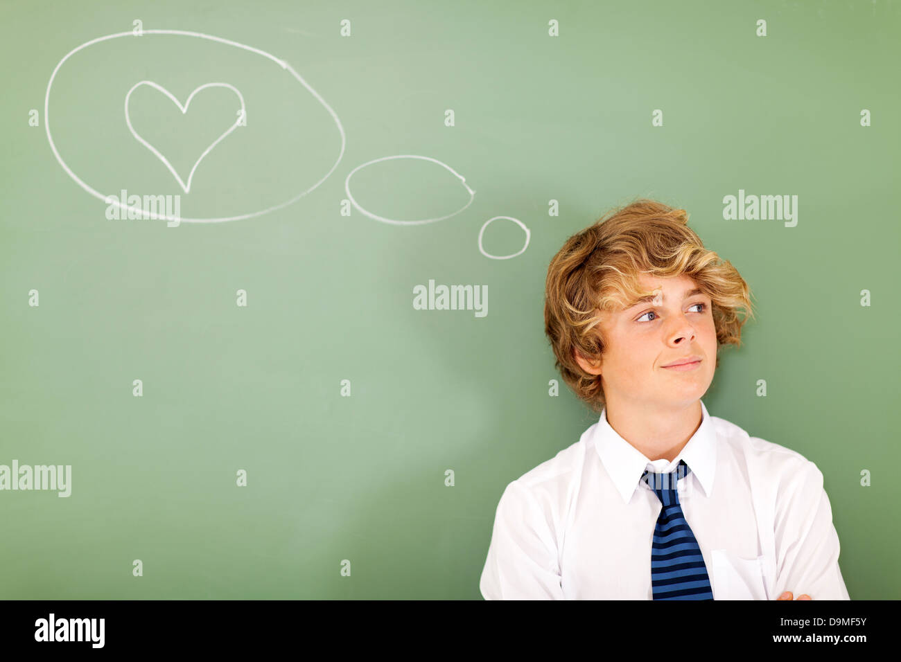 good looking teenage boy thinking about love in front of chalkboard ...