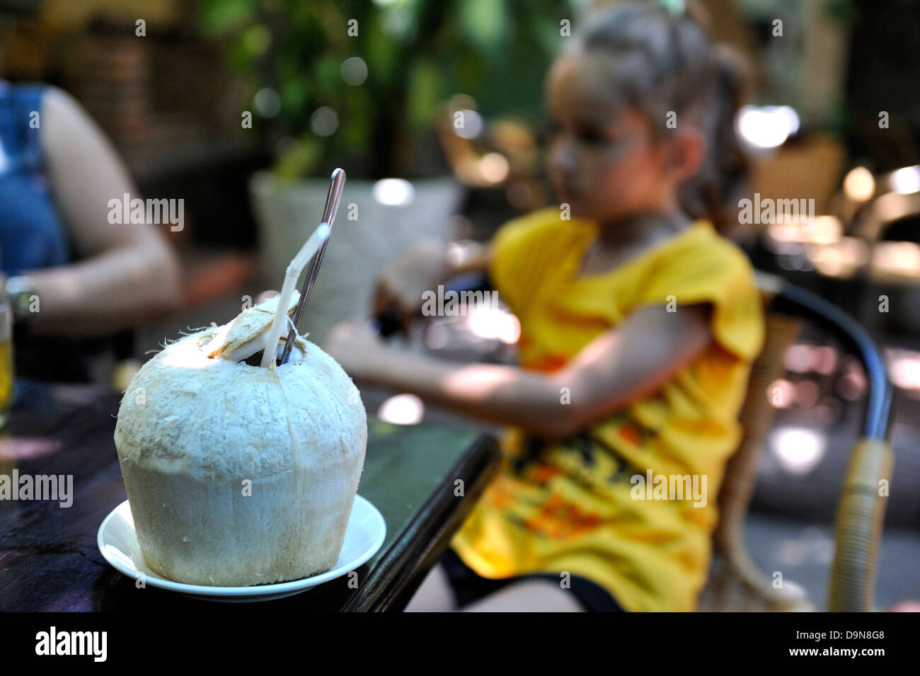 child sitting at table, with young, unripe coconut full of coconut ...