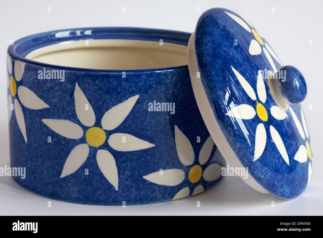Blue ceramic pot with daisies on with lid off and resting by the side ...