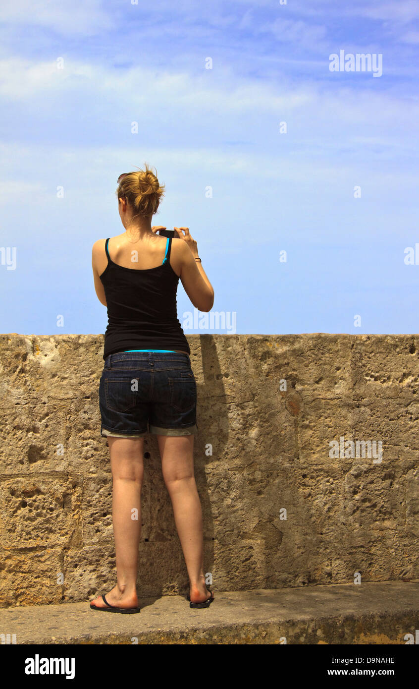 Blonde haired woman standing on a parapet looking over a wall admiring ...