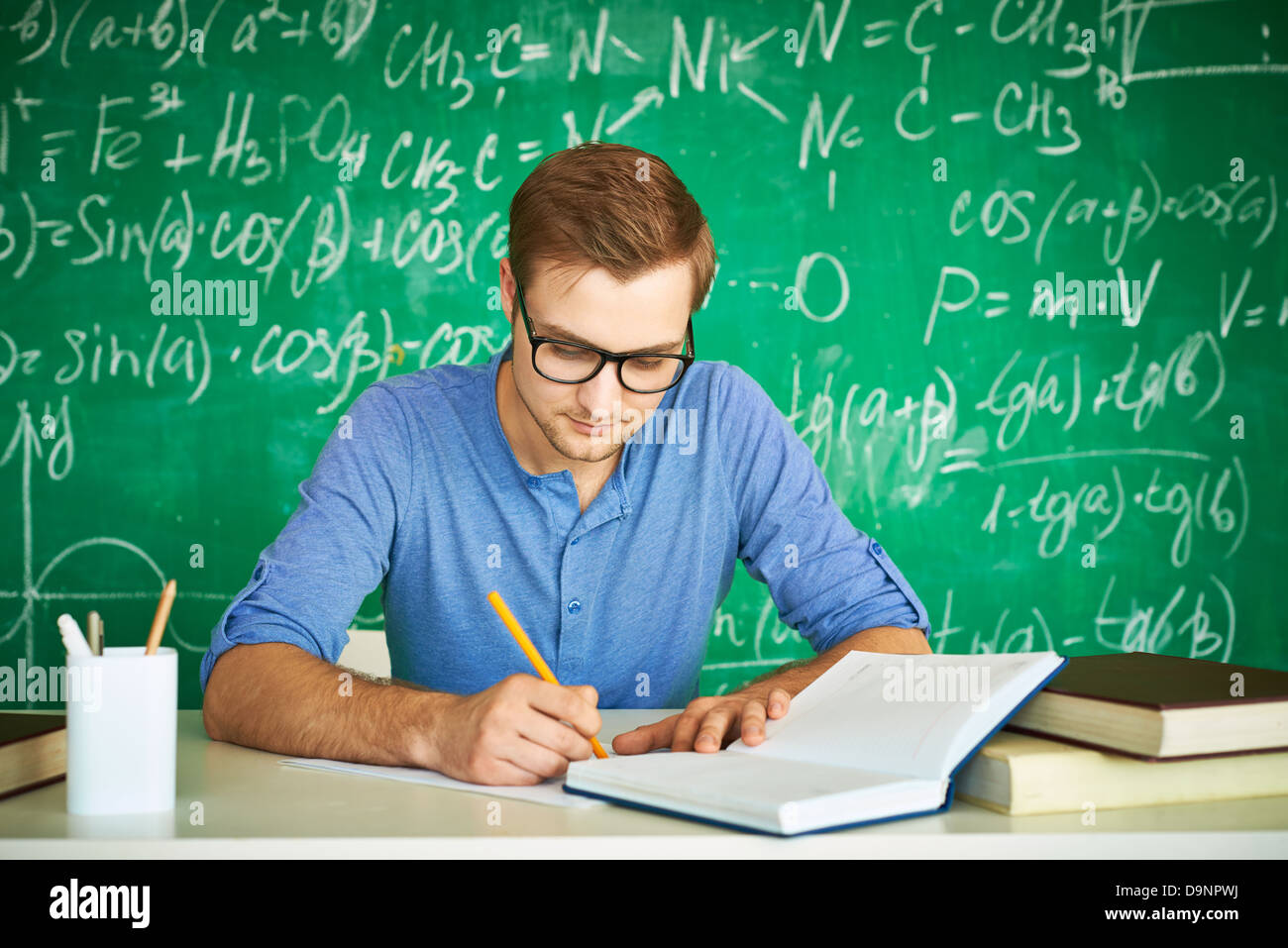 Portrait of handsome student carrying out graduation test on background ...