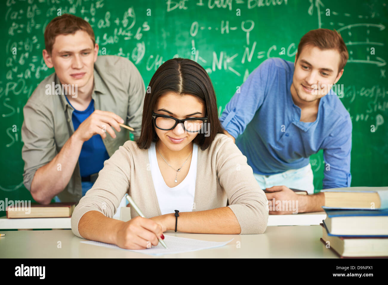 Portrait of smart student carrying out test with two guys behind ...
