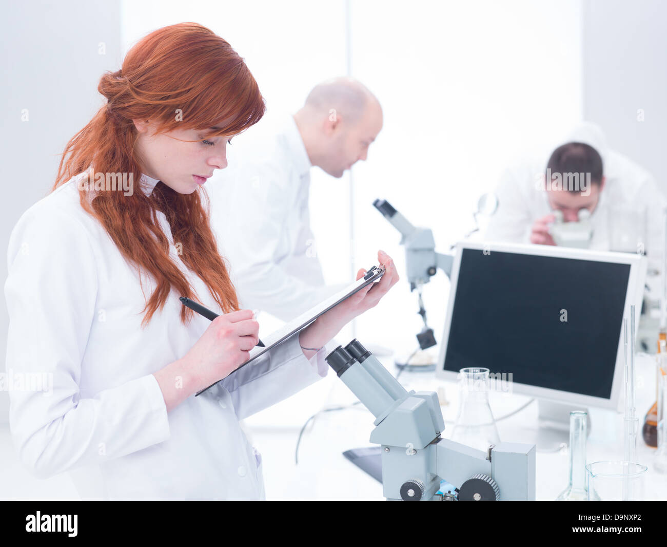 close-up of a student taking notes in a chemistry lab with another two ...