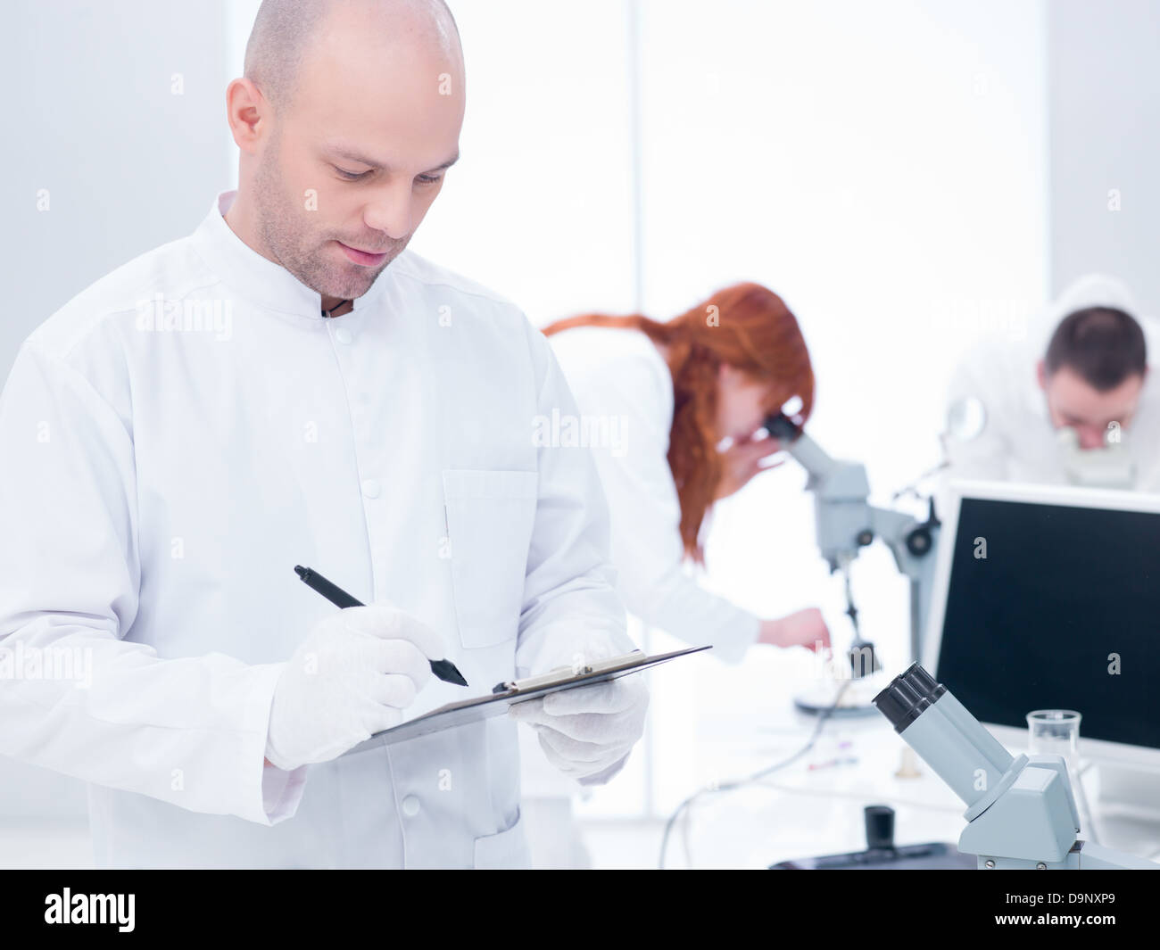 close-up of a scientist taking notes in a chemistry lab and another two ...