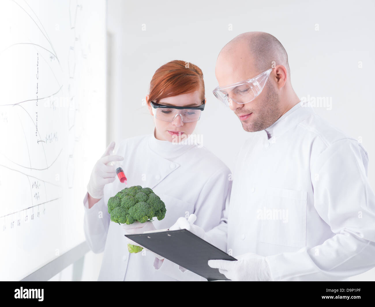 close-up of two people in a chemistry lab injecting a broccoli with a ...