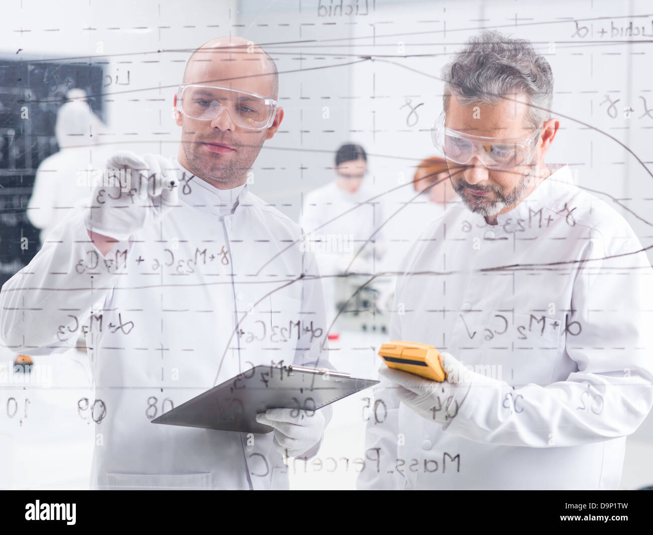 close-up of two researchers in a lab writing formulas on a transparent ...